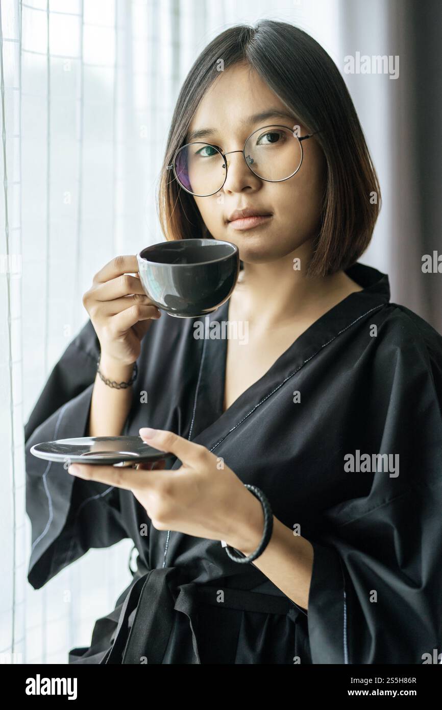 The woman wore a black robe near the window and drank coffee in the ...