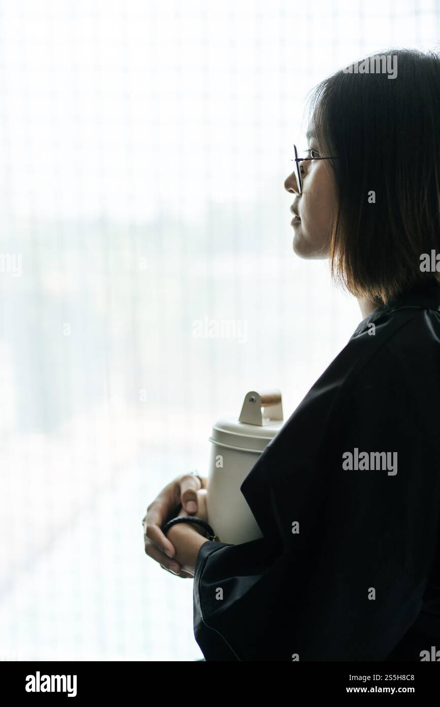 The woman wears a black robe and hugs tiffin and looks outside Stock ...