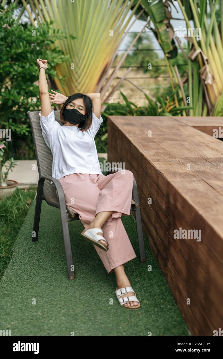 Woman wearing a face mask sitting on a chair beside a swimming pool in ...