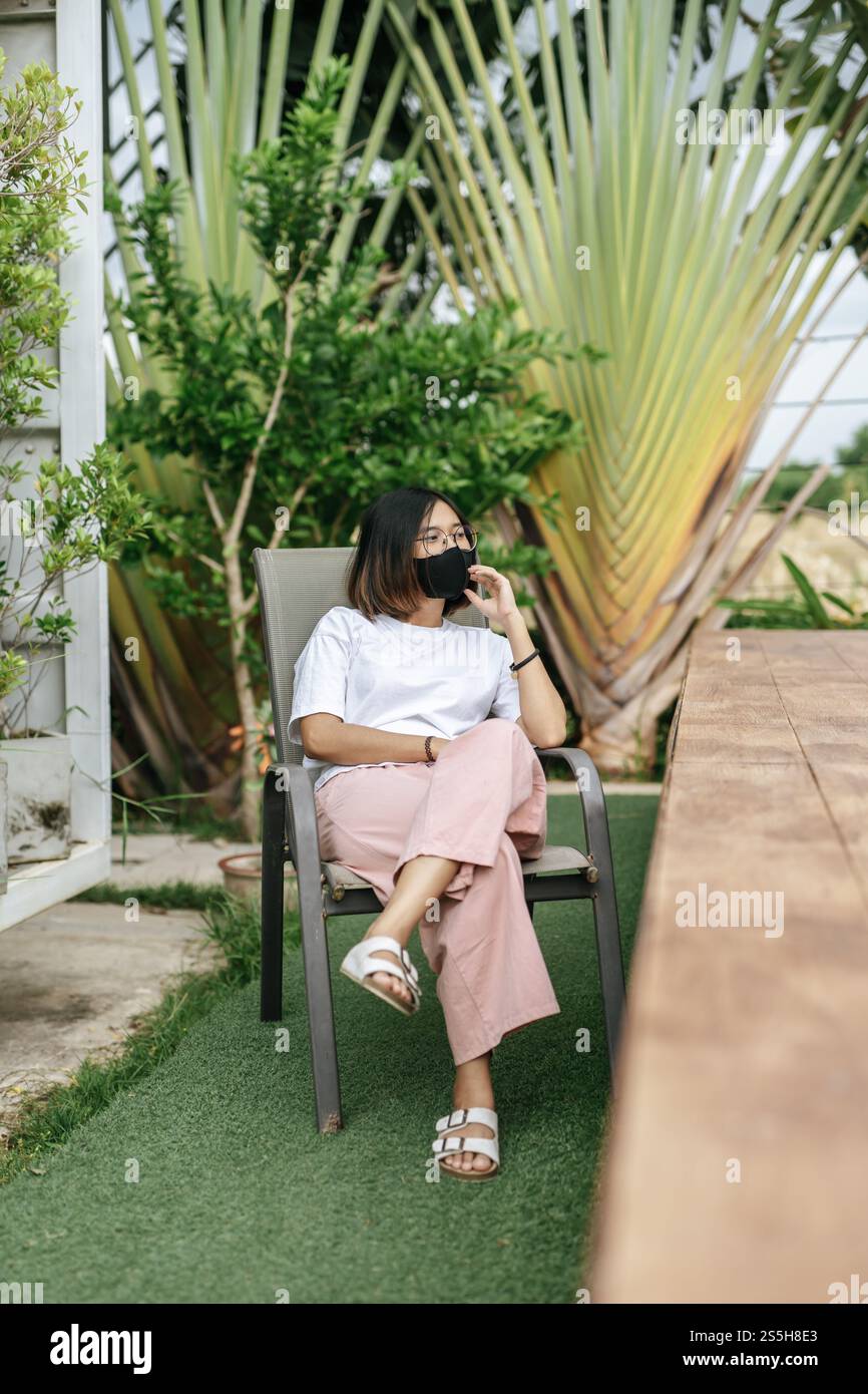Woman wearing a face mask sitting on a chair beside a swimming pool in ...