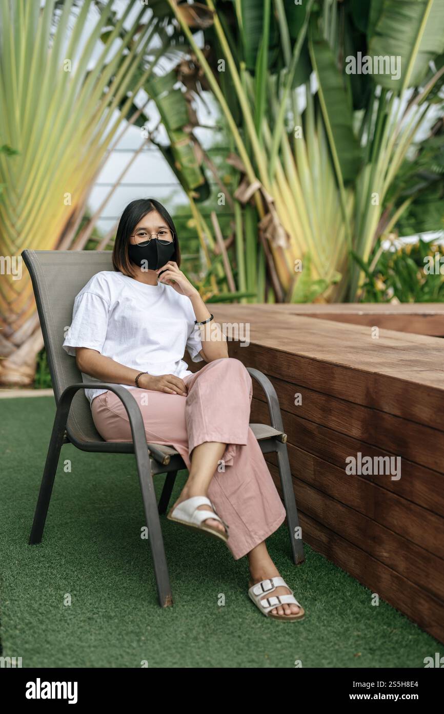 Woman wearing a face mask sitting on a chair beside a swimming pool in ...