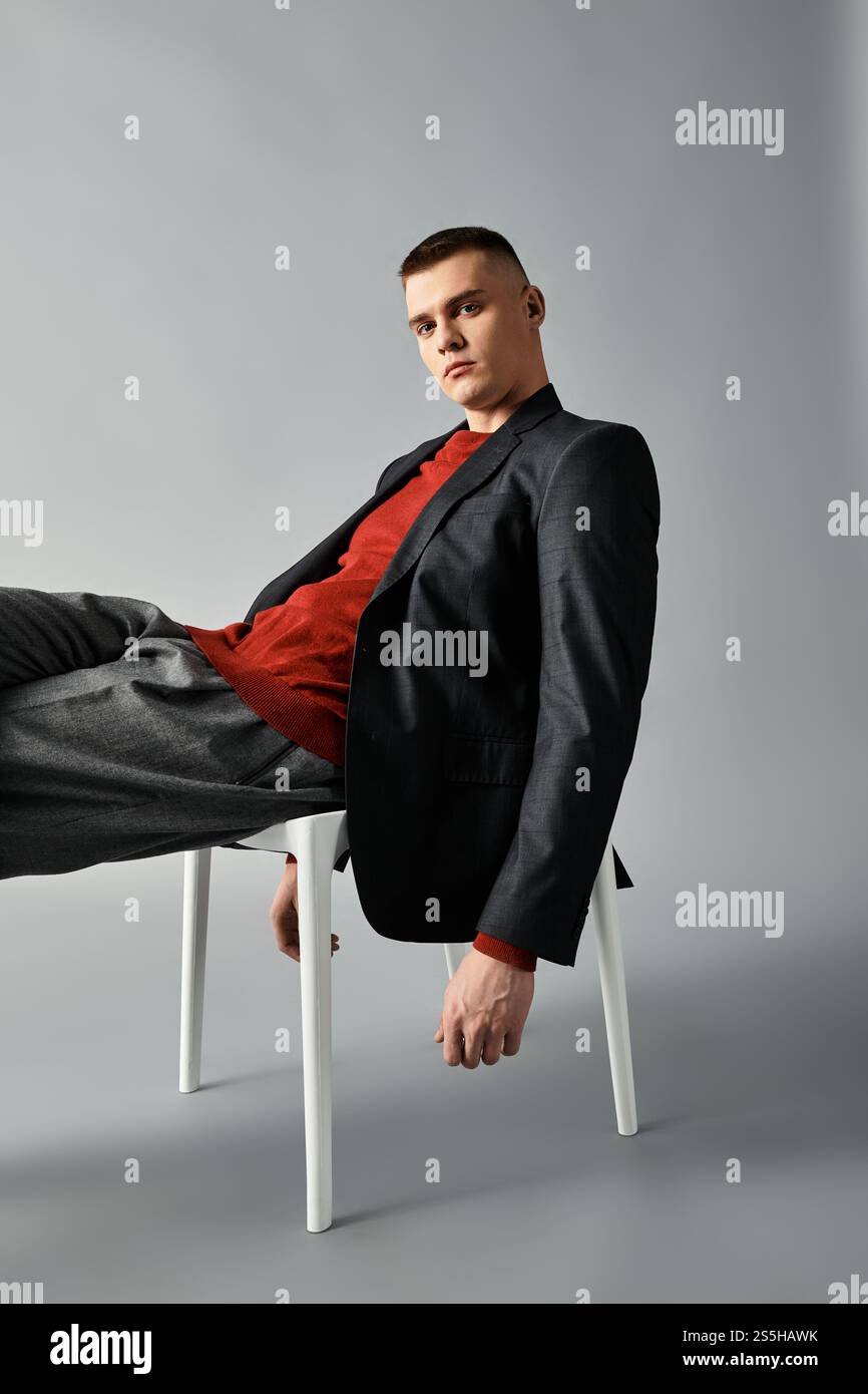 A young man in a stylish outfit leans casually on a white chair ...