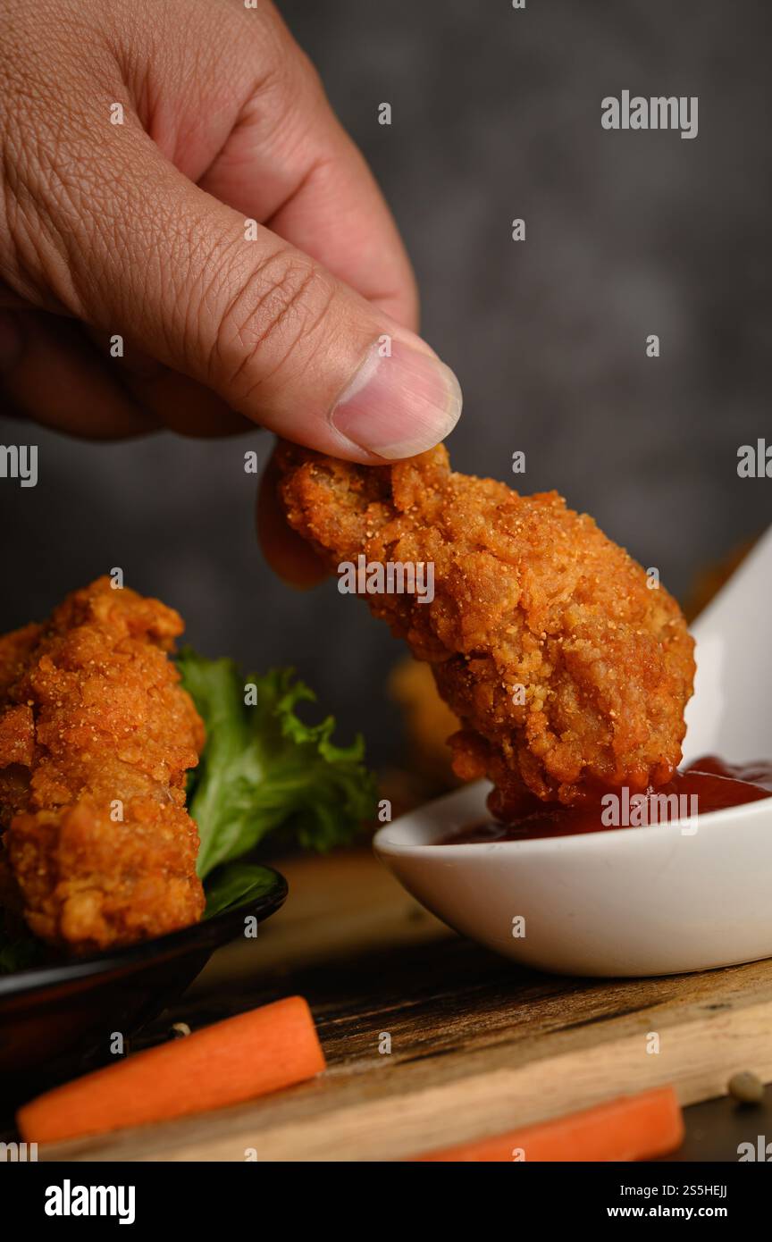 Hand holding crispy fried chicken dipped in tomato sauce. Selective ...