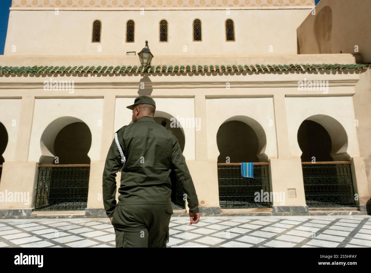 A police guard walking to a mosque with arabic architecture and moorish ...