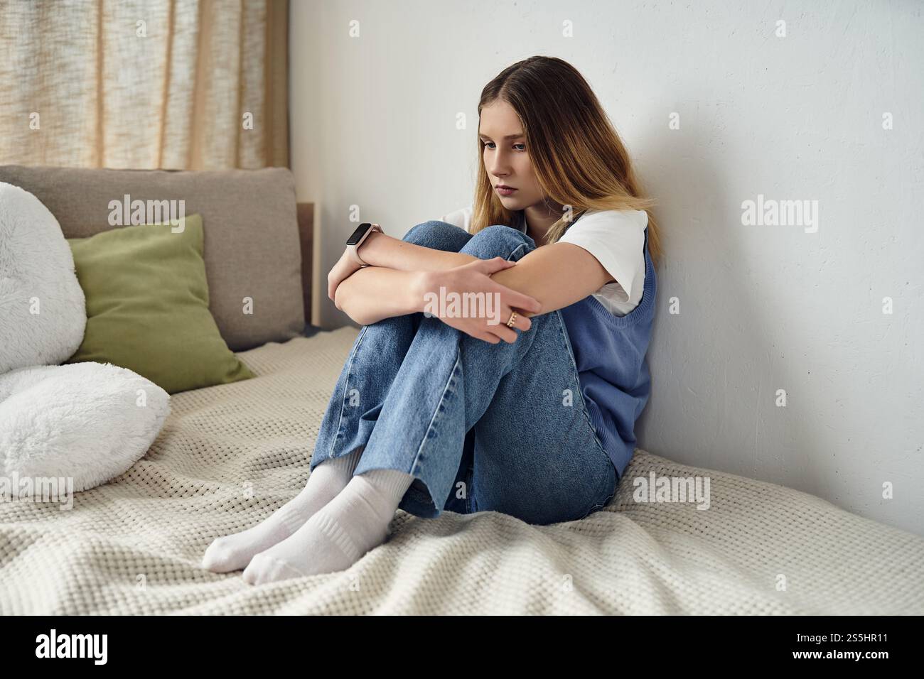 A teenager sits thoughtfully on her bed, surrounded by soft textures ...