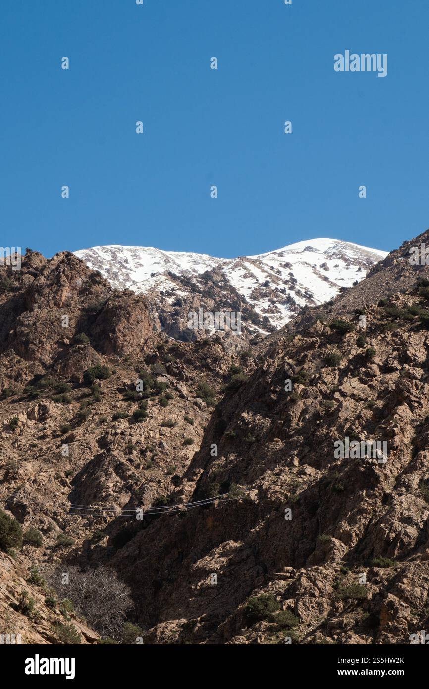 Peak of a snow mountain above the dirt mountains of the Ourika Valley ...
