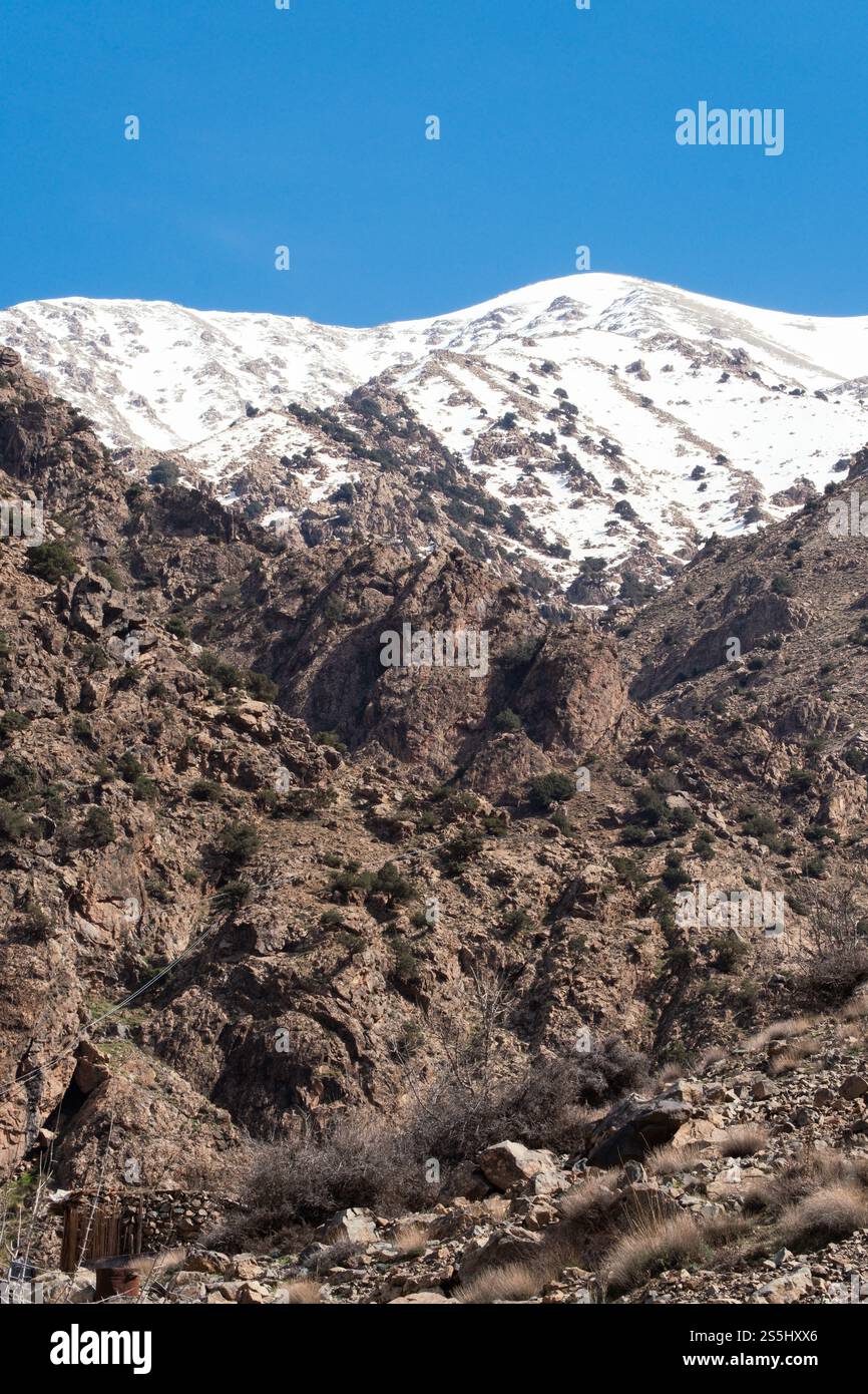Peak of a snow mountain above the dirt mountains of the Ourika Valley ...