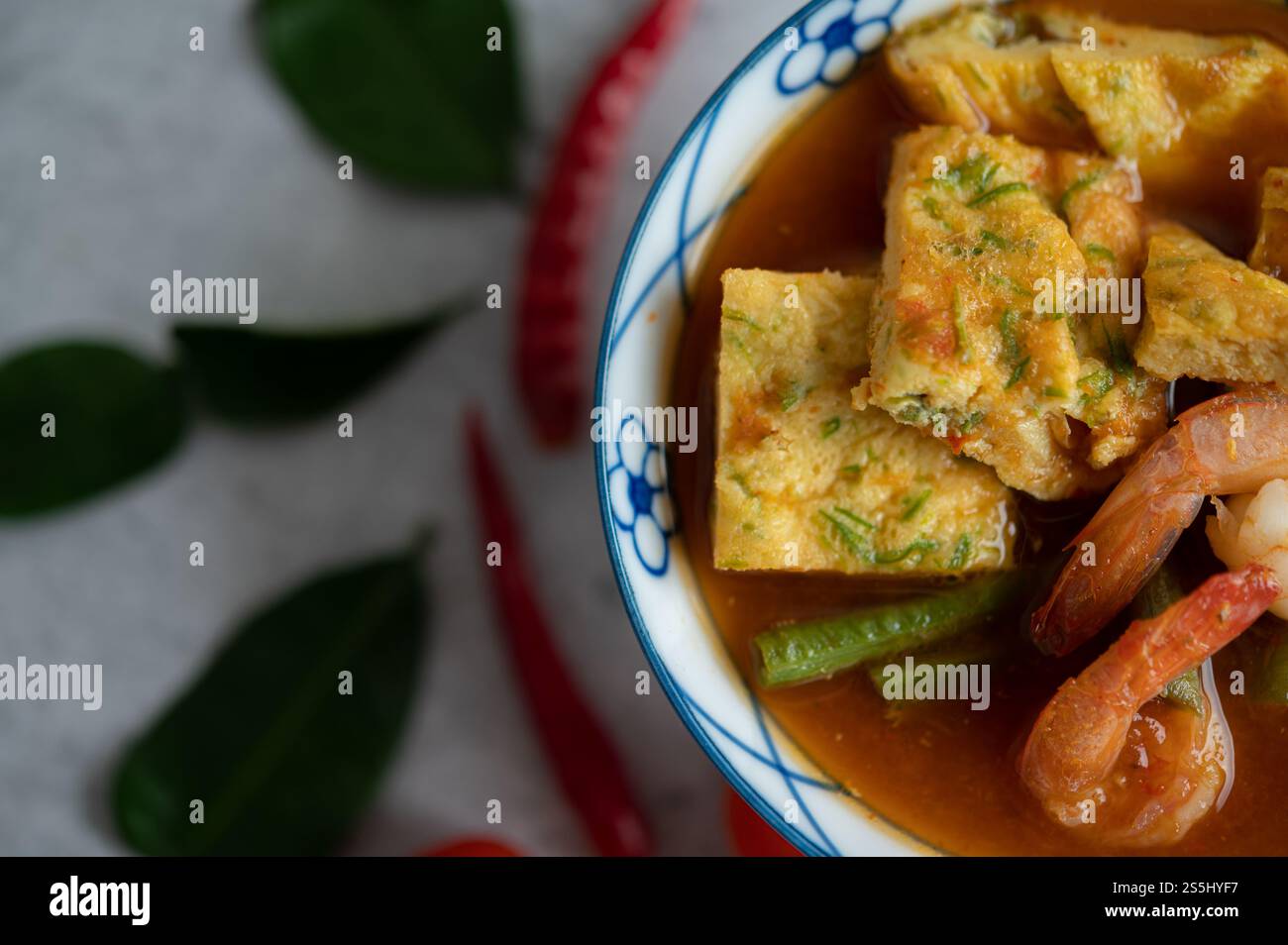 Hot and sour soup with cha-om, egg, and shrimp in a white bowl, with ...