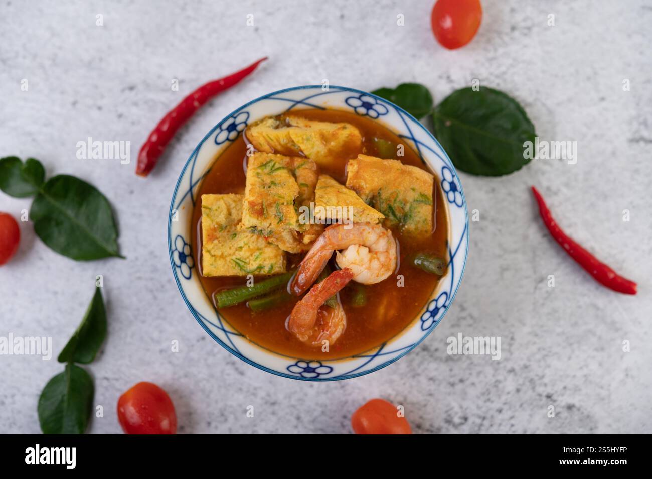 Hot and sour soup with cha-om, egg, and shrimp in a white bowl, with ...