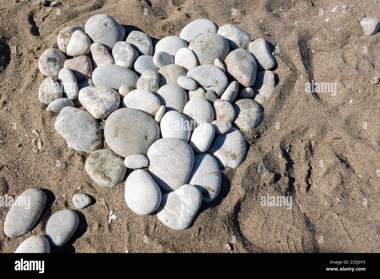 A heart shape made from smooth pebbles rests on the sand at the beach ...