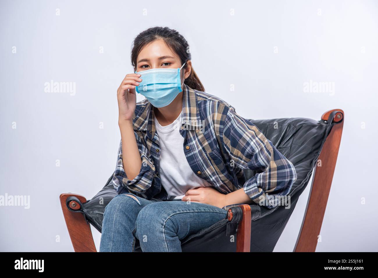 An uncomfortable woman sitting on a chair and wearing a mask Stock ...