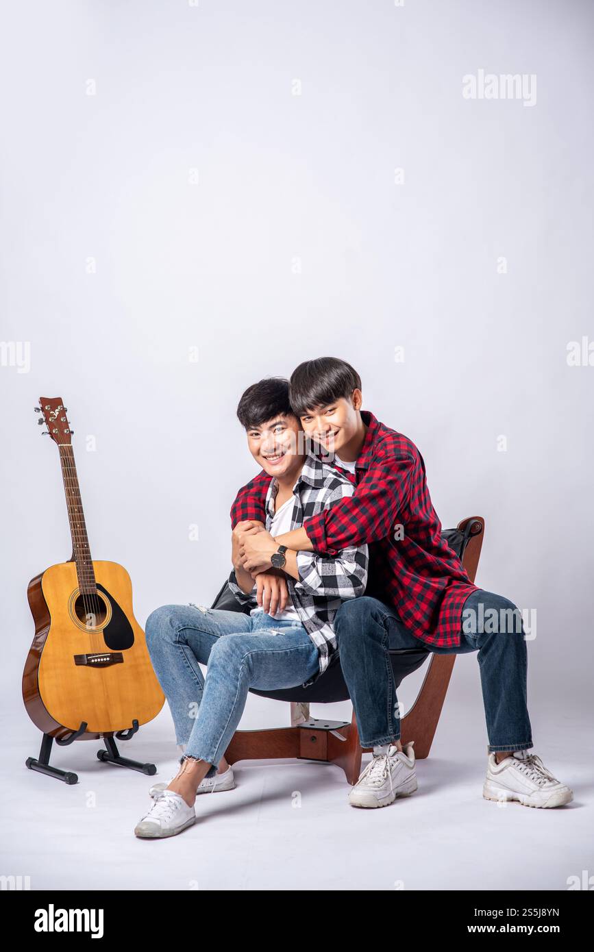 Two dear young men were sitting, cuddling in a chair, and with a guitar ...
