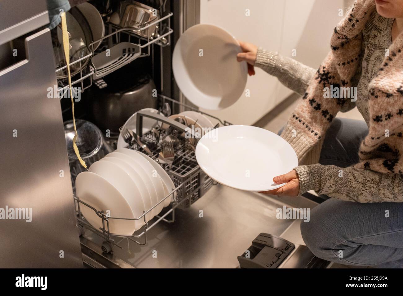 Woman loading clean dishes into dishwasher at home in cozy kitchen ...