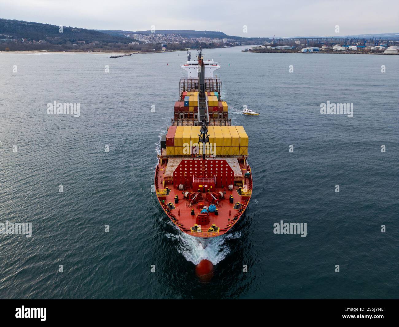 Front aerial view of a red container ship sailing through calm waters ...