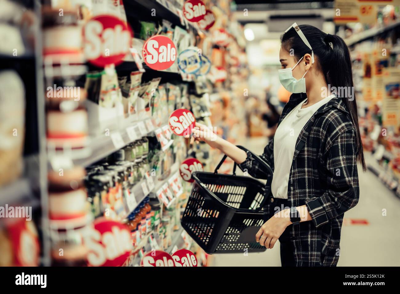 Young woman in protection mask holding basket and standing to choose ...