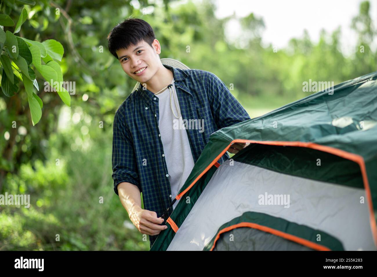 Smiley Young traveler man setting a tent on the camping in the forest ...