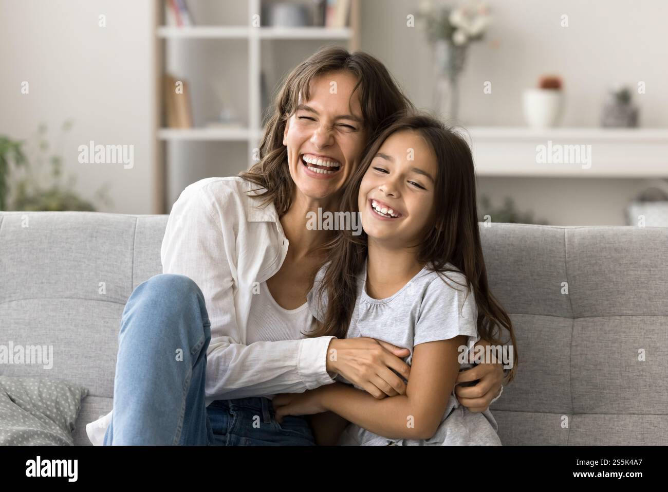 Laughing mother cuddling her little daughter seated on cozy couch Stock ...