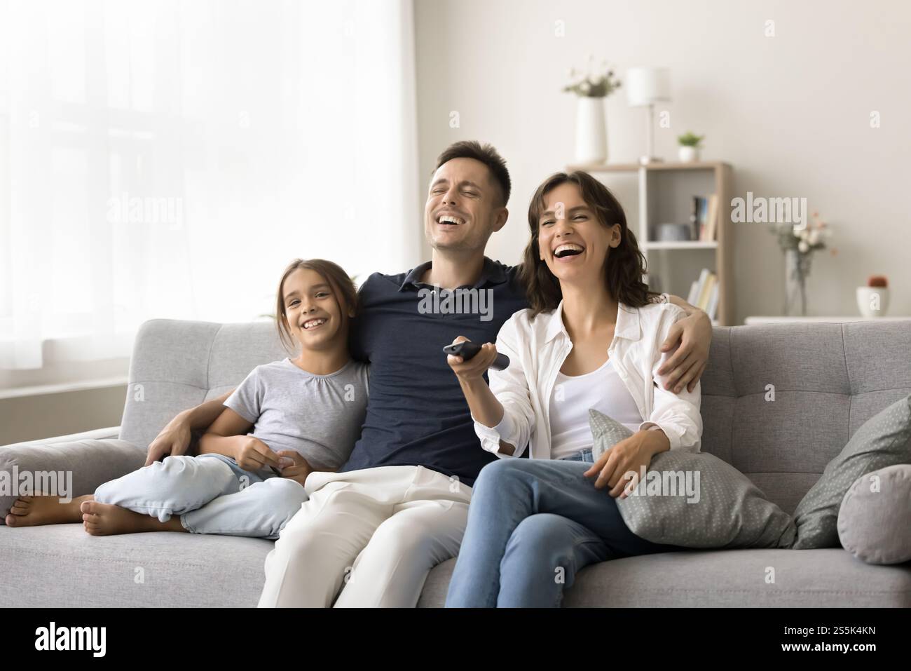 Happy parents with daughter sitting watching favourite television show ...