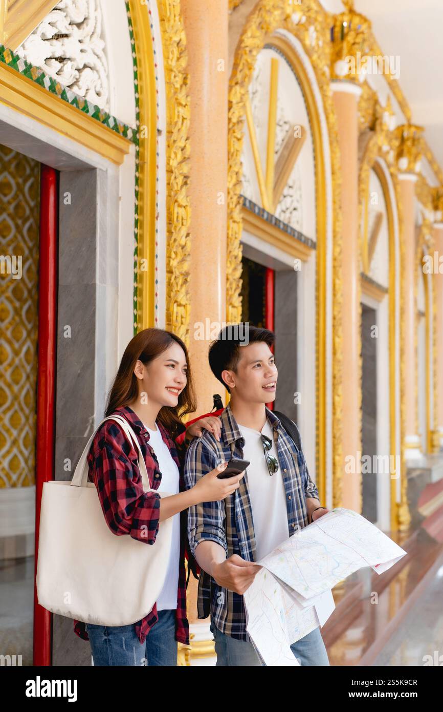 Smiley Asian couple tourist backpackers standing in beautiful Thai temple, pretty woman holding ...