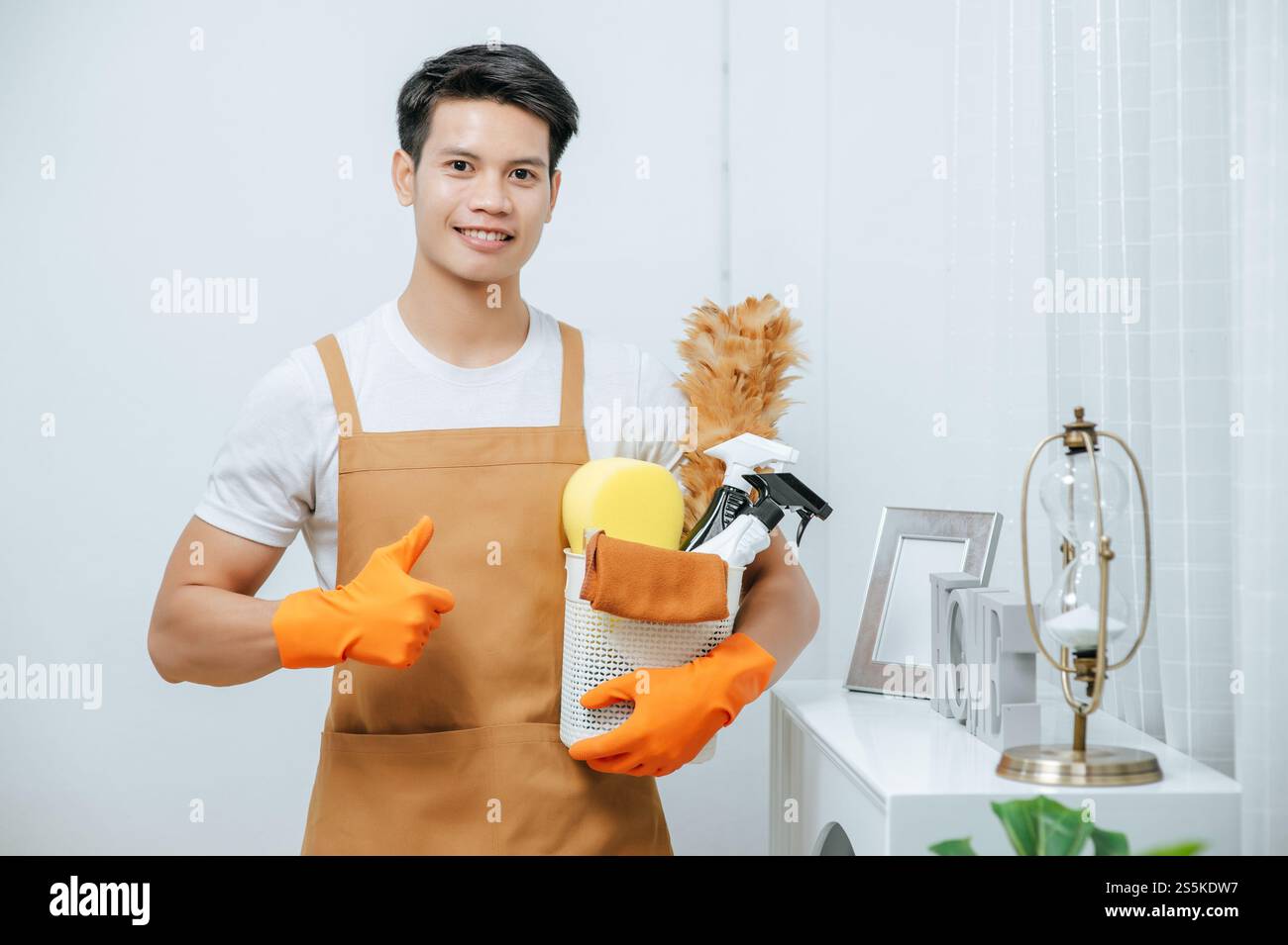 Portrait Young housekeeper man in apron and rubber gloves holding a ...