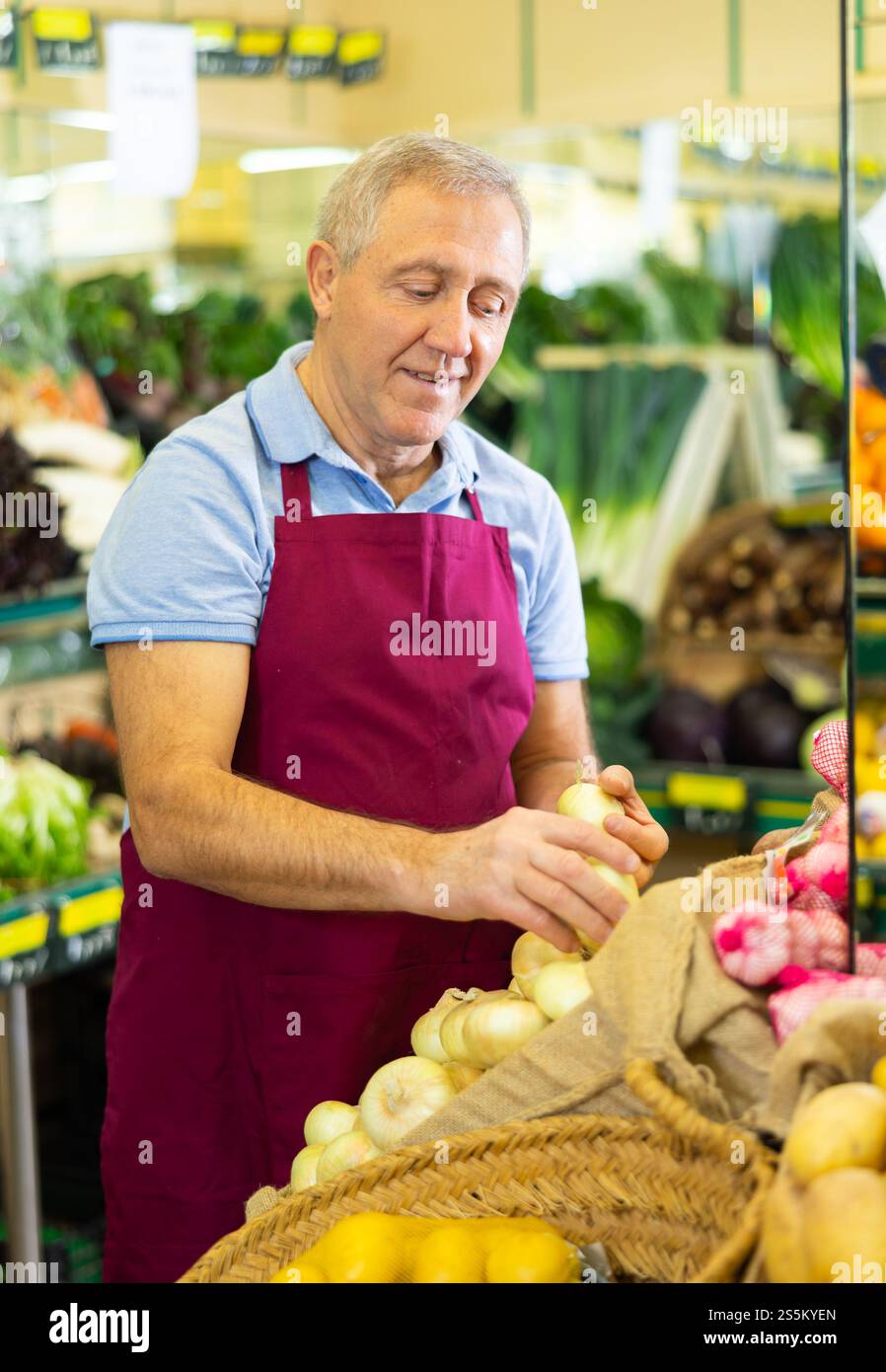 Aged salesman putting onions on food stall in greengrocery Stock Photo ...