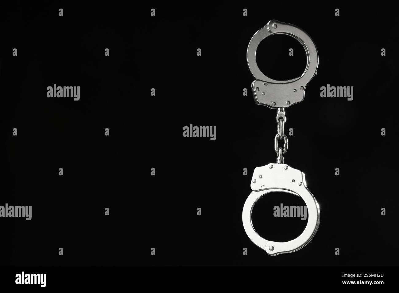 Metal chain handcuffs on black background, closeup. Space for text ...
