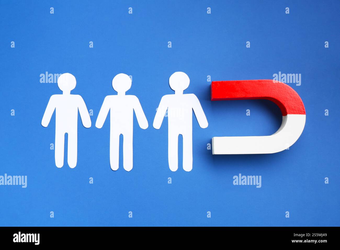 Magnet attracting paper human figures on blue background, top view ...