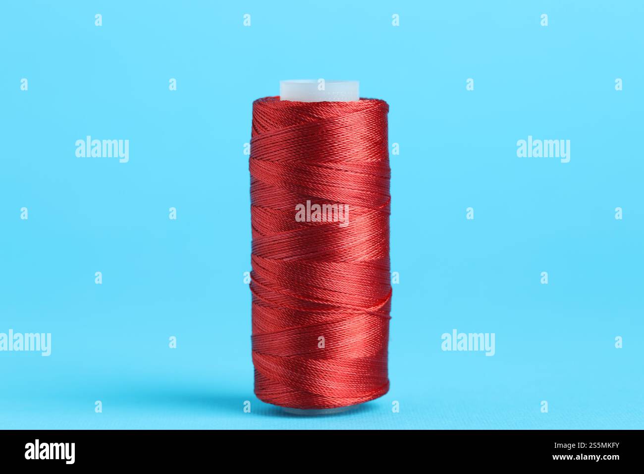 Spool of red sewing thread on light blue background Stock Photo - Alamy