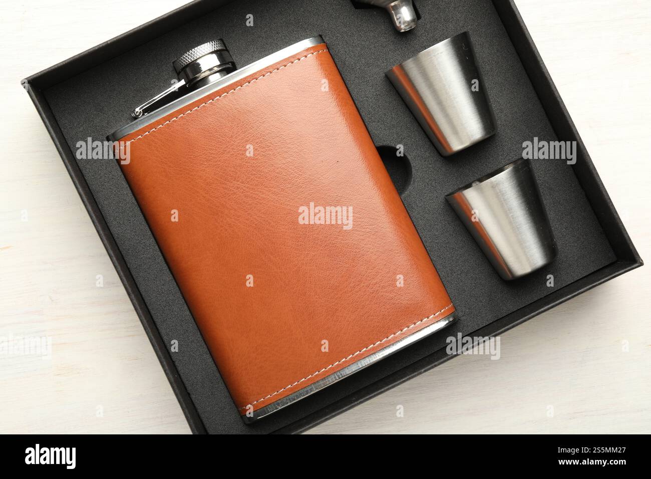 Hip flask, cups and funnel in package on light wooden table, top view ...