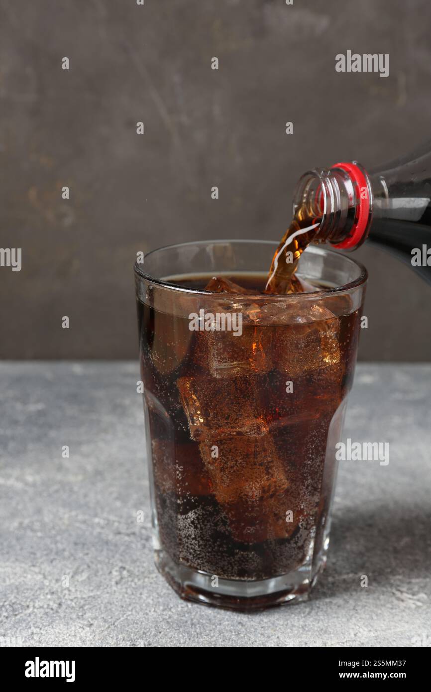 Pouring refreshing cola from bottle into glass on light textured table ...