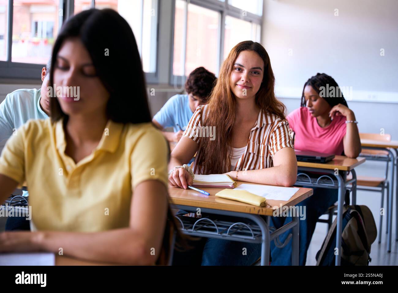 Portrait European young woman student sitting at desk with classmates ...