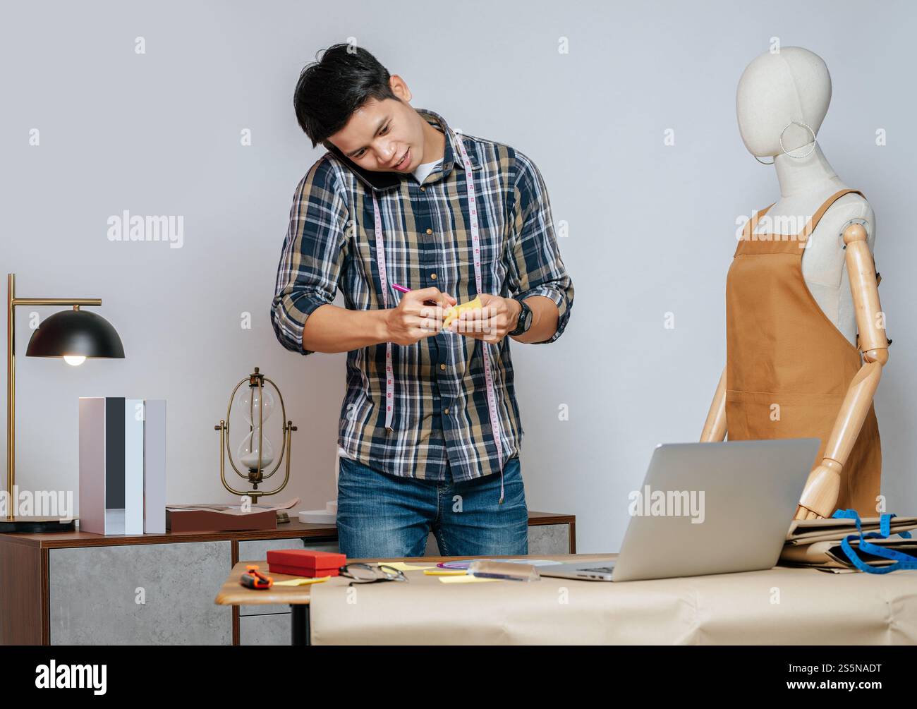 young Asian fashion designer or tailor working with laptop computer ...