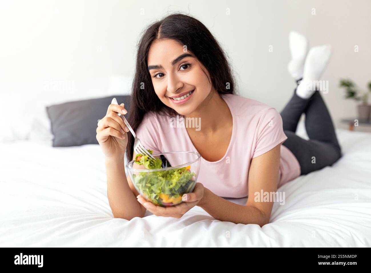 Healthy eating, dieting and detox concept. Pretty Indian woman having fresh veggie salad, lying ...