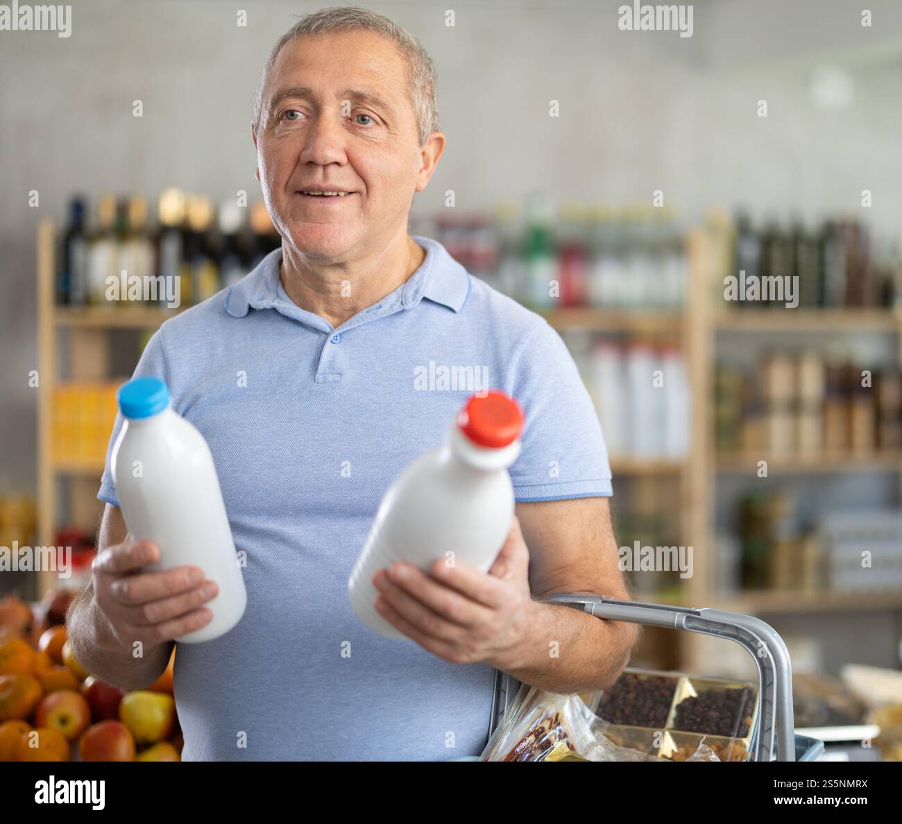 Mature man hold white plastic bottles and choose consider milk in store ...