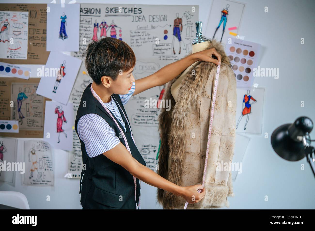 Charming female tailor using the tape measure on the mannequin to cut ...