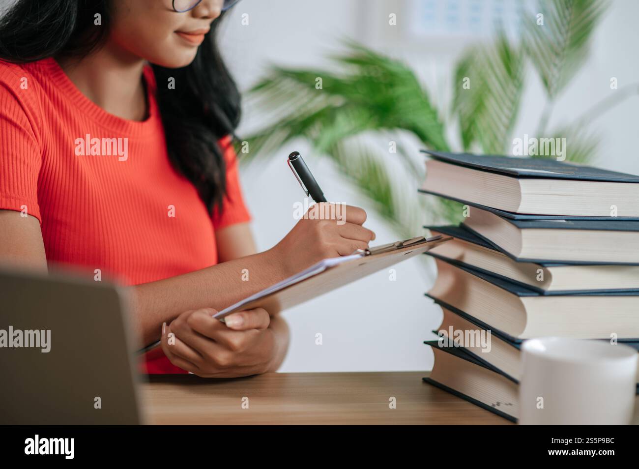 Woman holding checklist in office and stack of books on table Stock ...