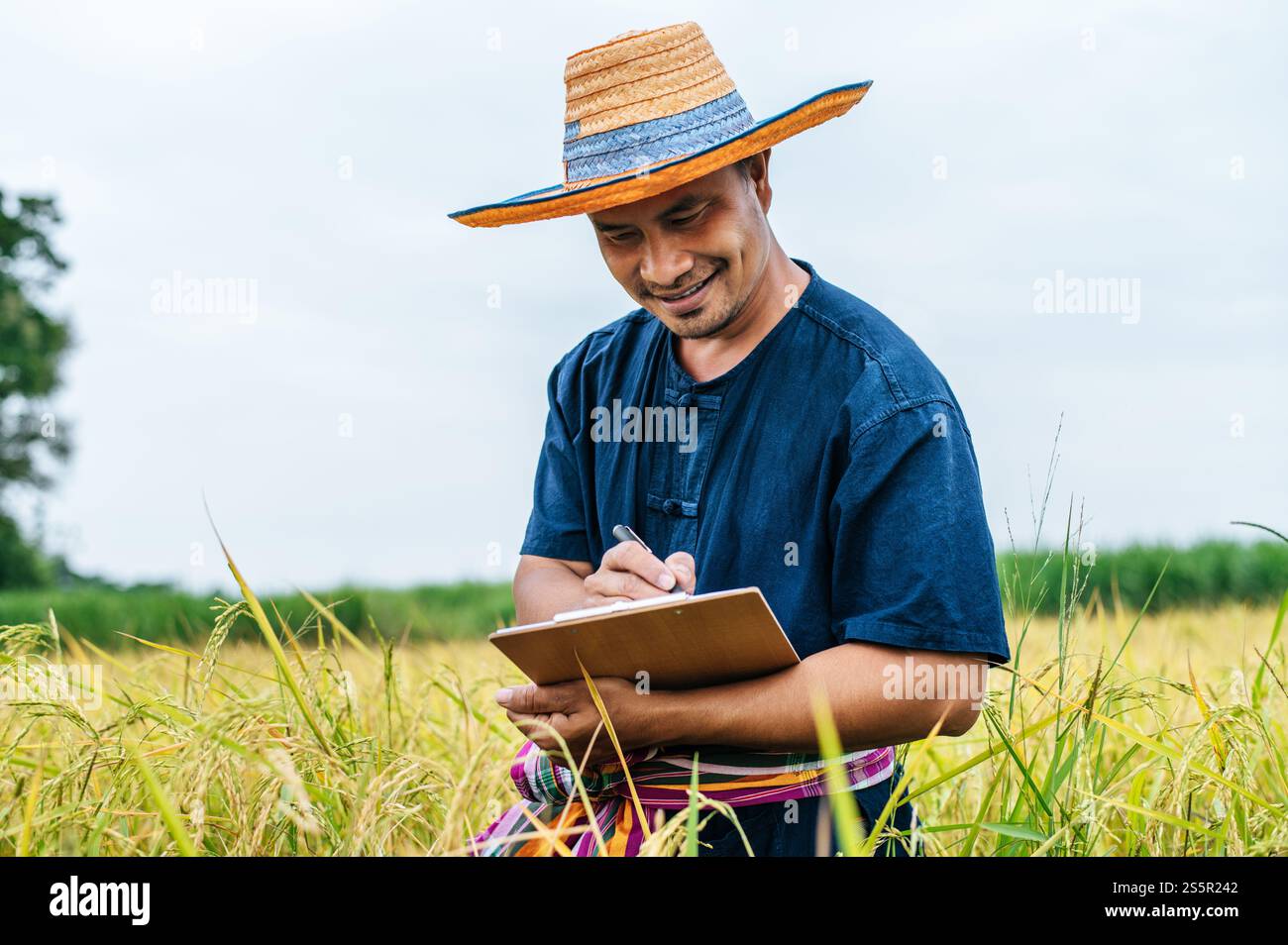 Asian middle aged farmer man wearing straw hat write on clipboard in ...