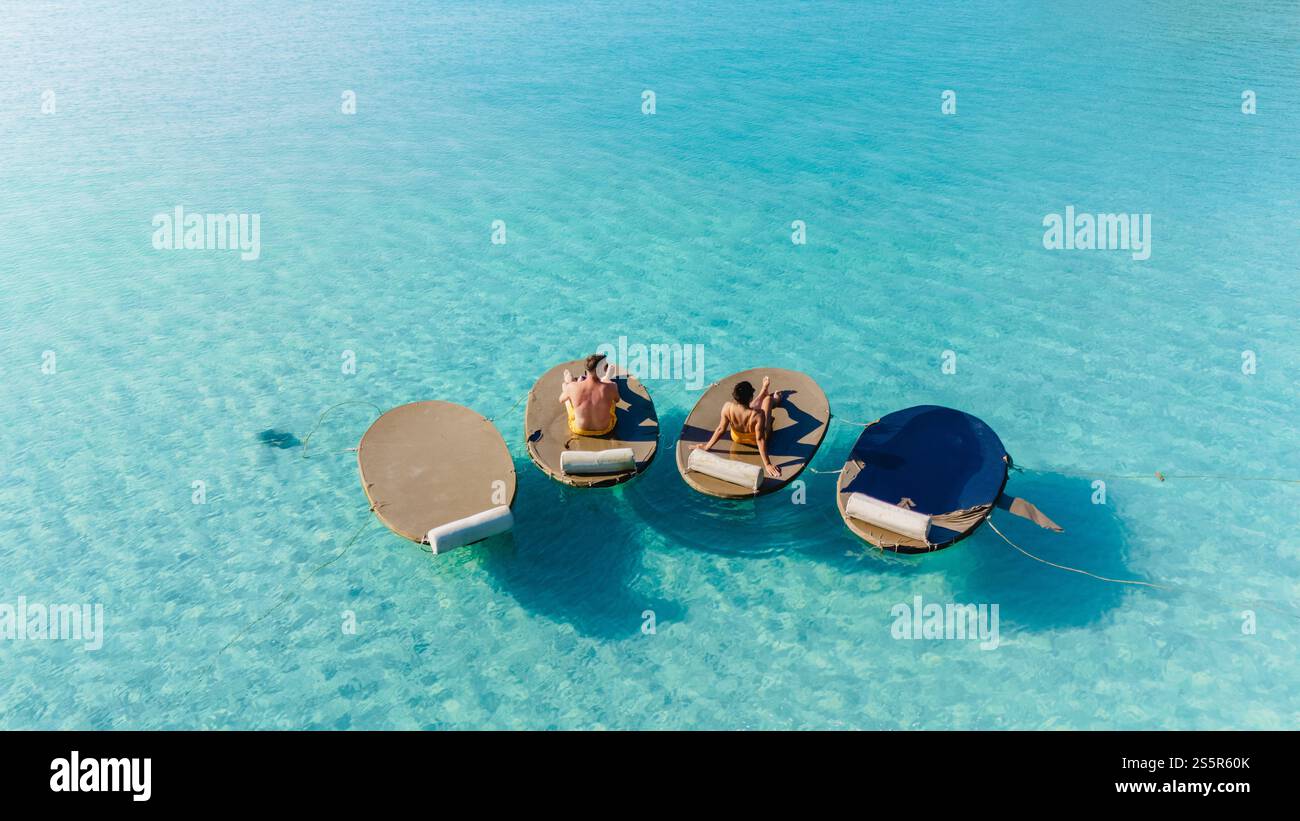 A couple of men and women enjoy a serene day, lounging on floating beds ...