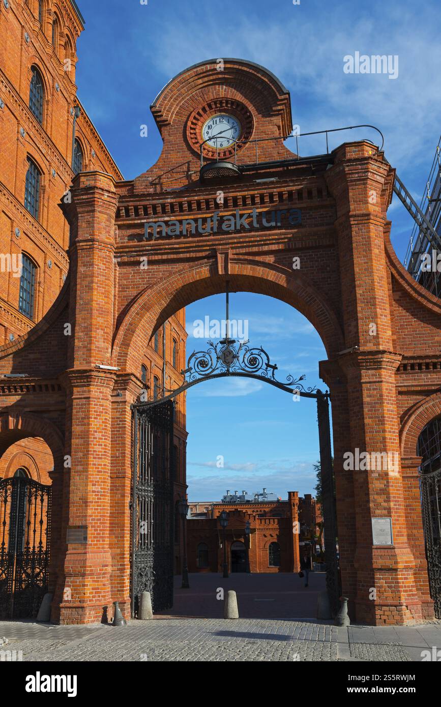 A historic brick gate with a clock, in front of a building in daylight ...
