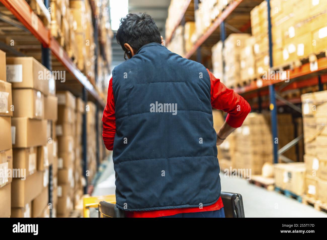 Rear view of a latin male worker pushing an hydraulic hand pallet truck ...
