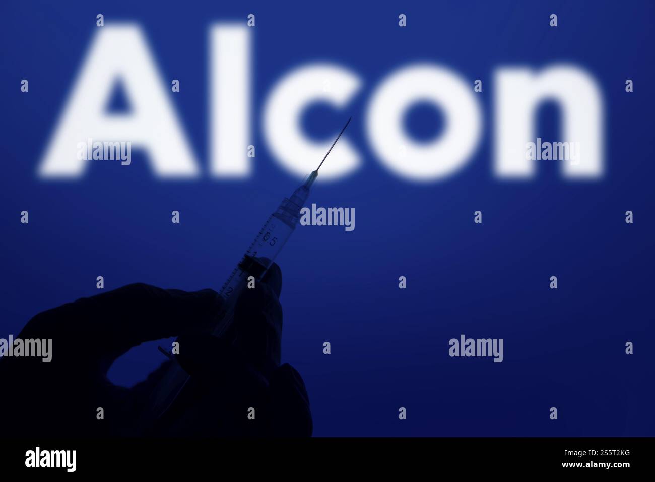 A gloved hand holding a syringe in front of the Alcon logo. Alcon Inc ...