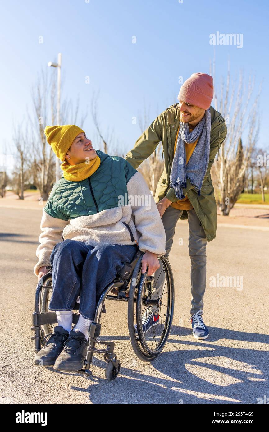 Caregiver pushing his disabled friend in a wheelchair, enjoying a sunny ...