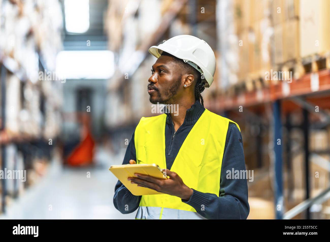 African male warehouse worker taking inventory looking away with ...