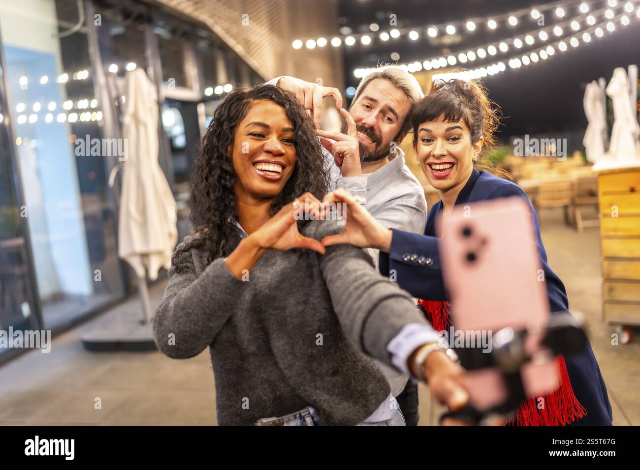 Multi-ethnic friends join hands gesturing heart shape while vlogging ...