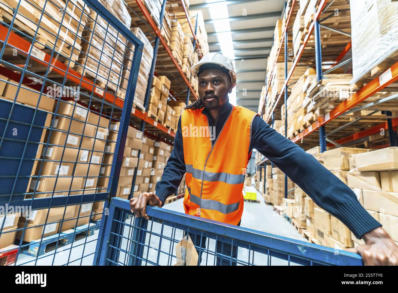 African worker pushing a metallic cart in a distribution warehouse ...