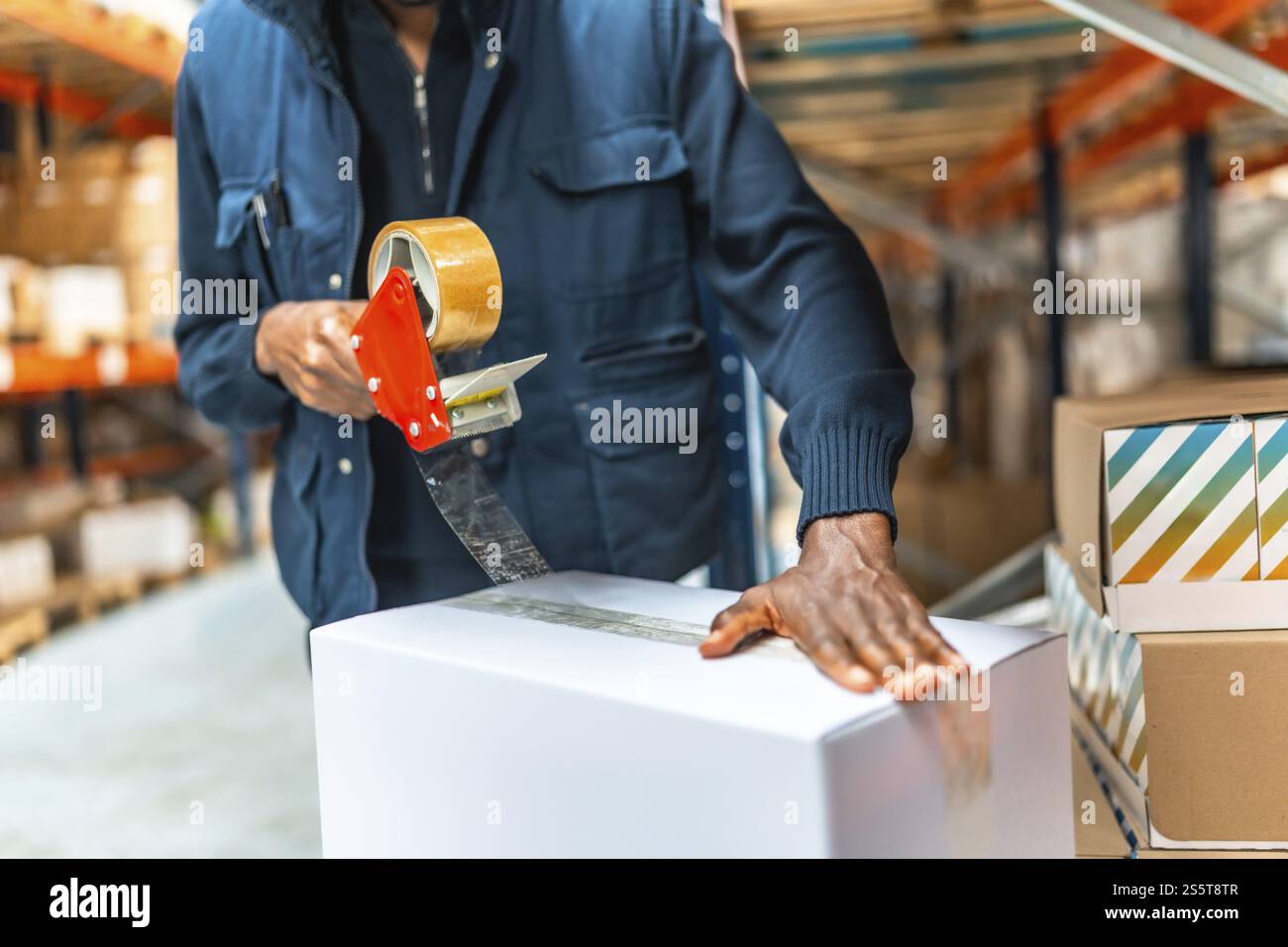 Close-up of an african man using tape gun to close boxes to deliver at ...