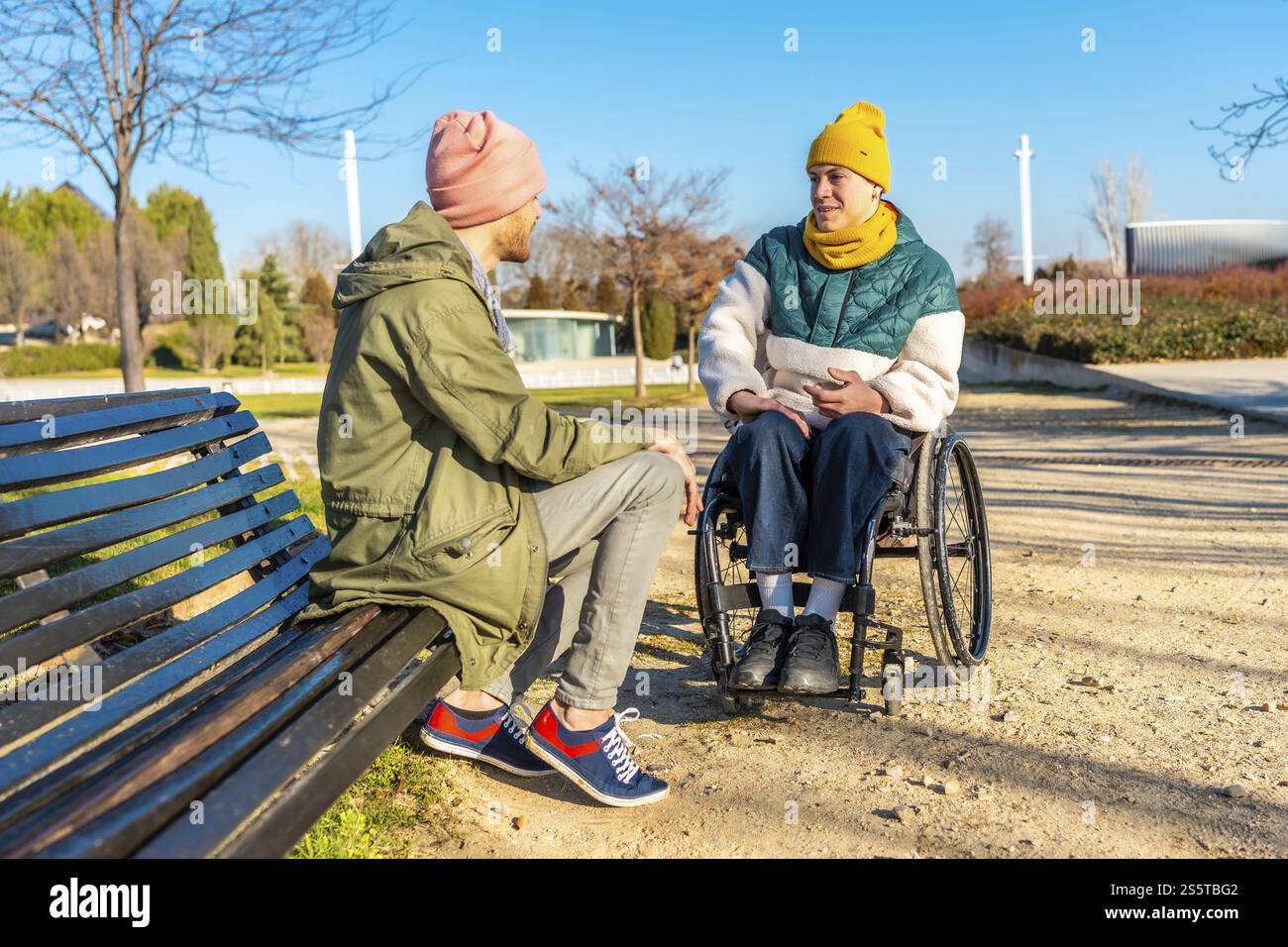 Two young men enjoying conversation on sunny winter day in park ...