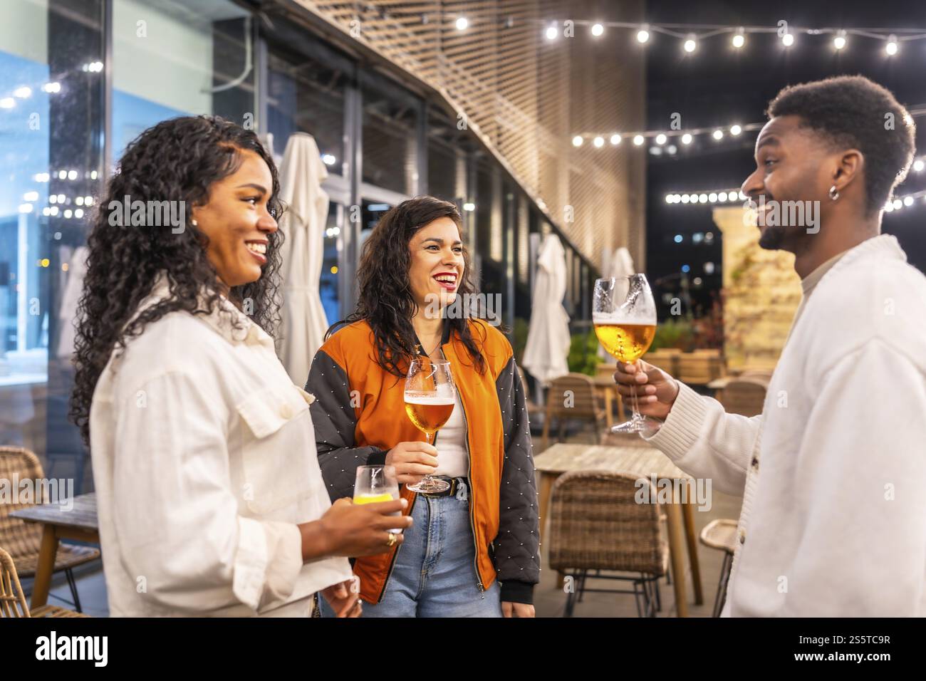 Multi-ethnic friends talking while drinking beer at night in an elegant ...