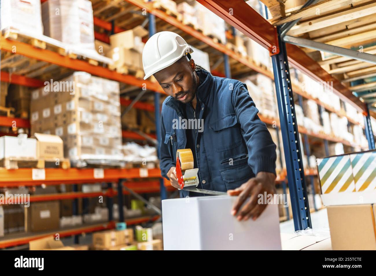 Male african employee working at a distribution warehouse closing boxes ...