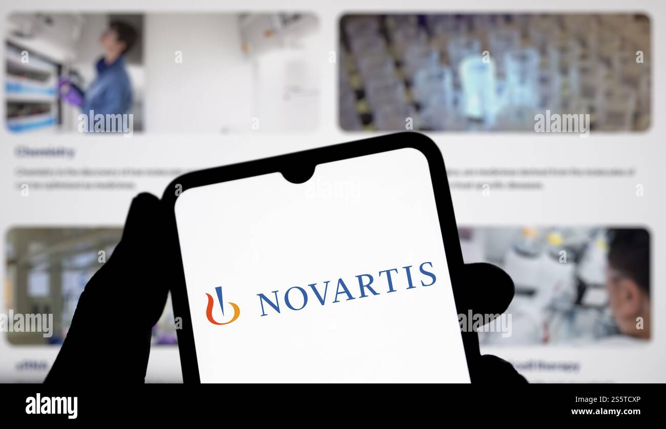 A gloved hand holding a syringe in front of the Novartis logo. Novartis ...
